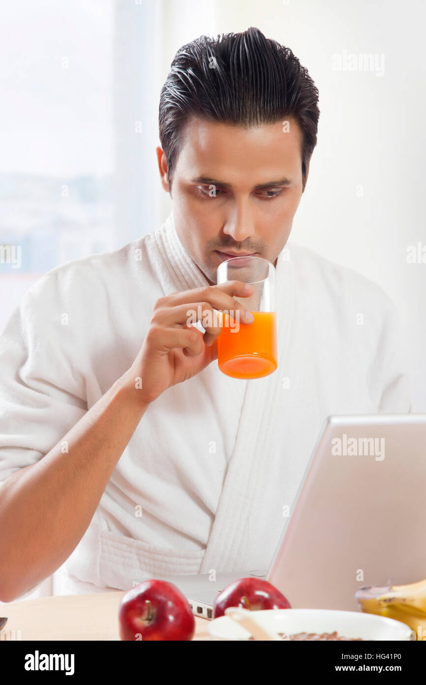 Man drinking juice while using laptop at breakfast table Stock Photo ...