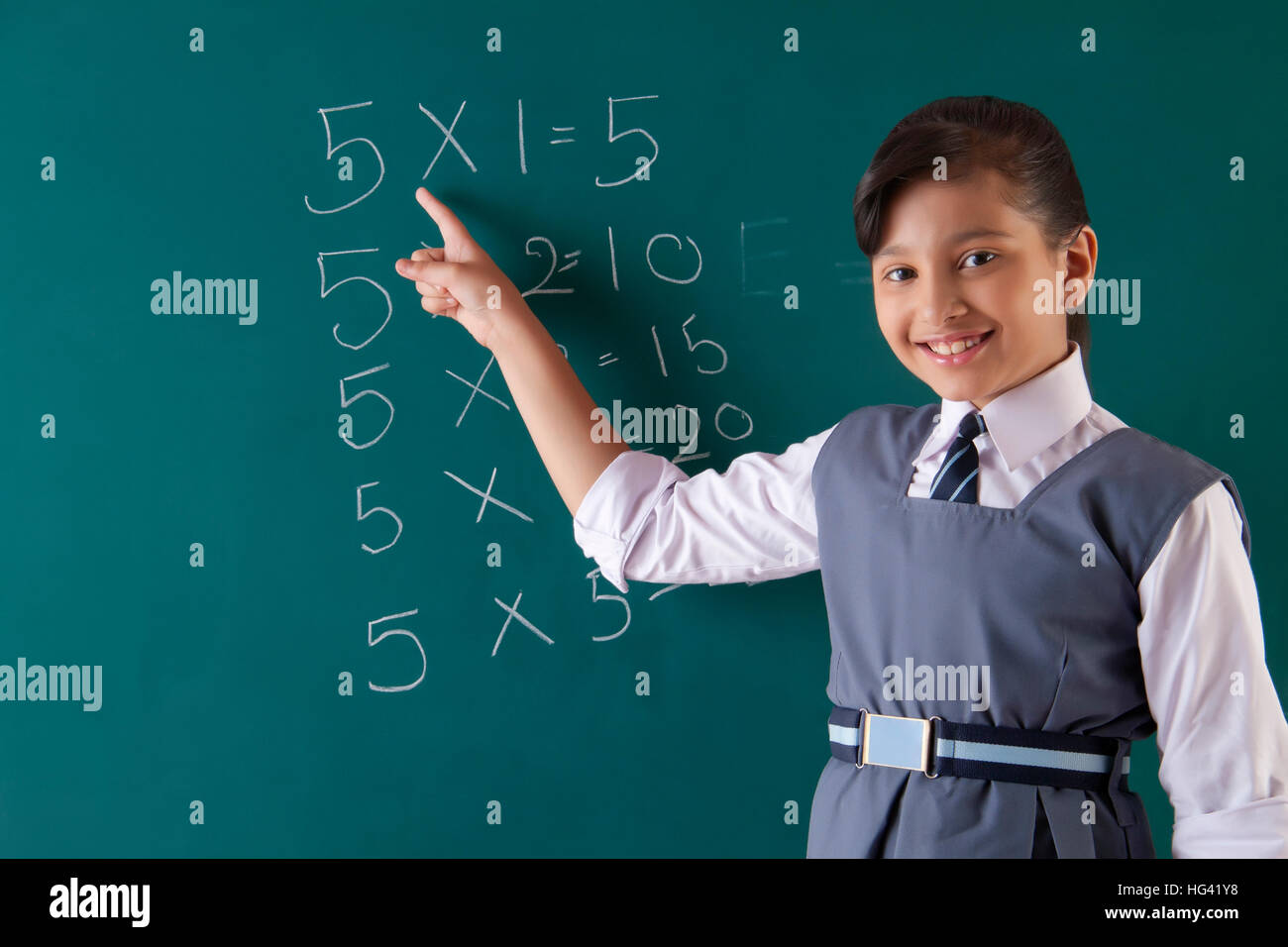Smiling Girl pointing at tables written on blackboard in a classroom ...