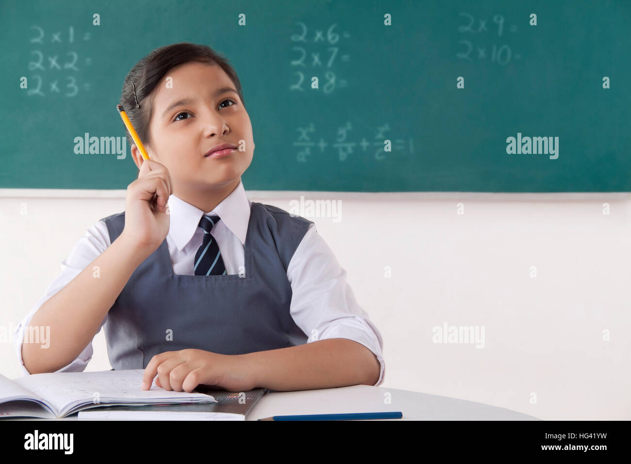 Girl thinking while writing notes in a classroom Stock Photo - Alamy