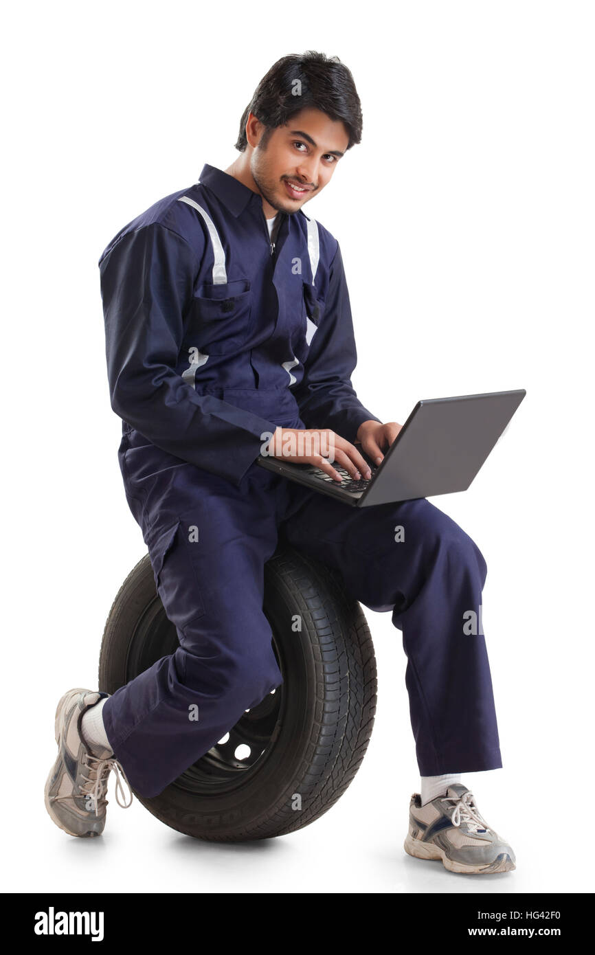 Car mechanic sitting on tyre and using laptop Stock Photo - Alamy