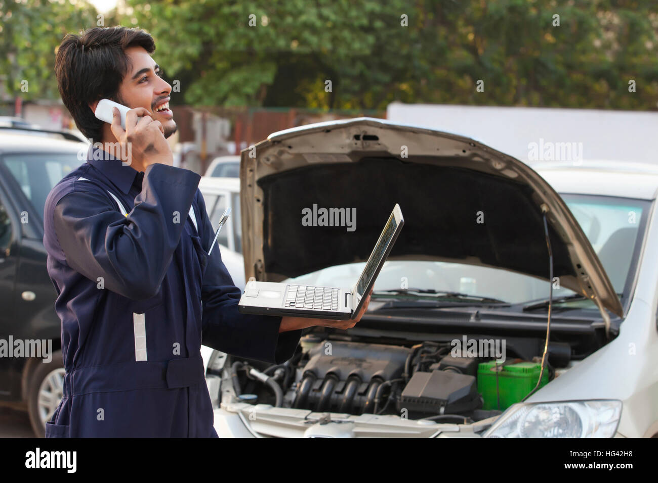Mechanic talking on phone while using laptop on car engine Stock Photo ...