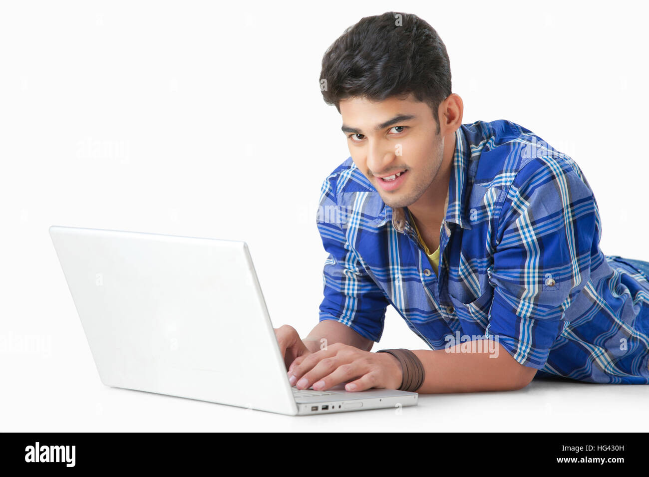 Happy Indian man lying on floor using a laptop PC looking at camera ...