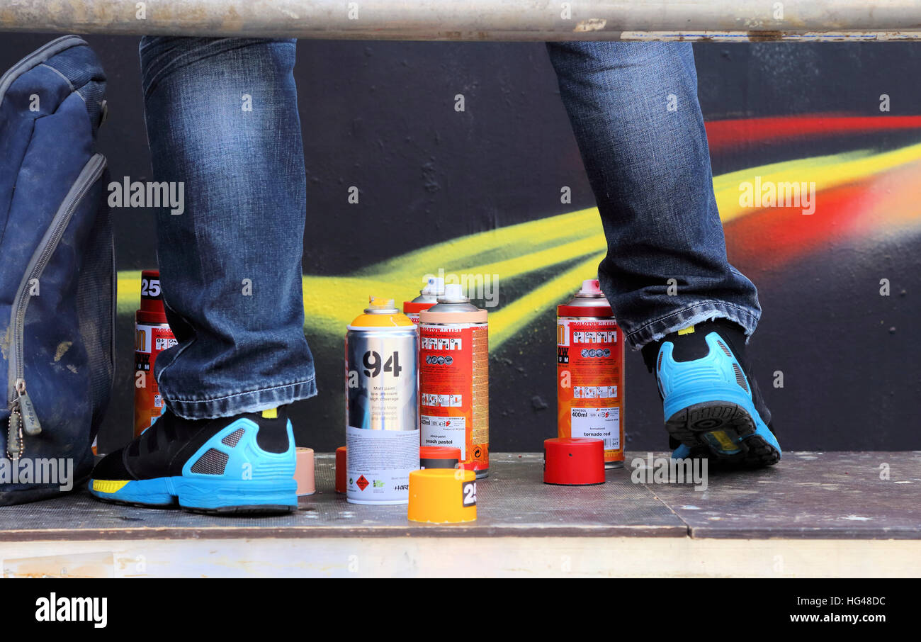 The legs of a graffiti artist standing on a platform whilst working on ...