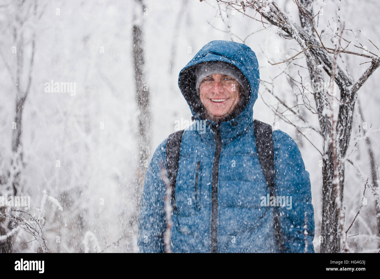 Young handsome man standing in snowfall on background of snowy forest ...