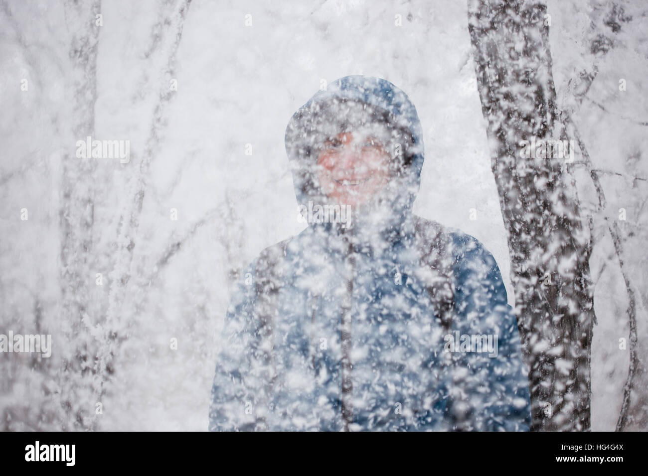 Young handsome man standing in snowfall on background of snowy forest ...
