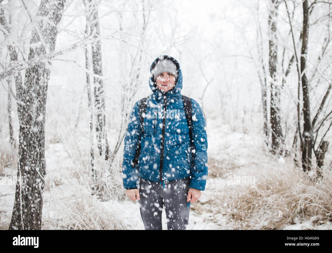 Young handsome man standing in snowfall on background of snowy forest ...