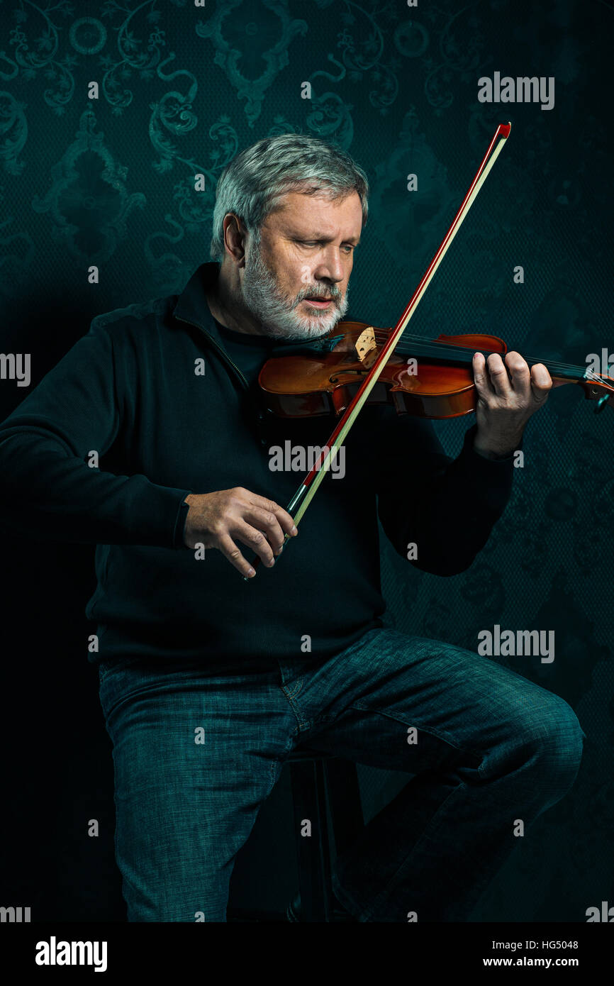 Senior musician playing a violin with a wand on black studio background ...
