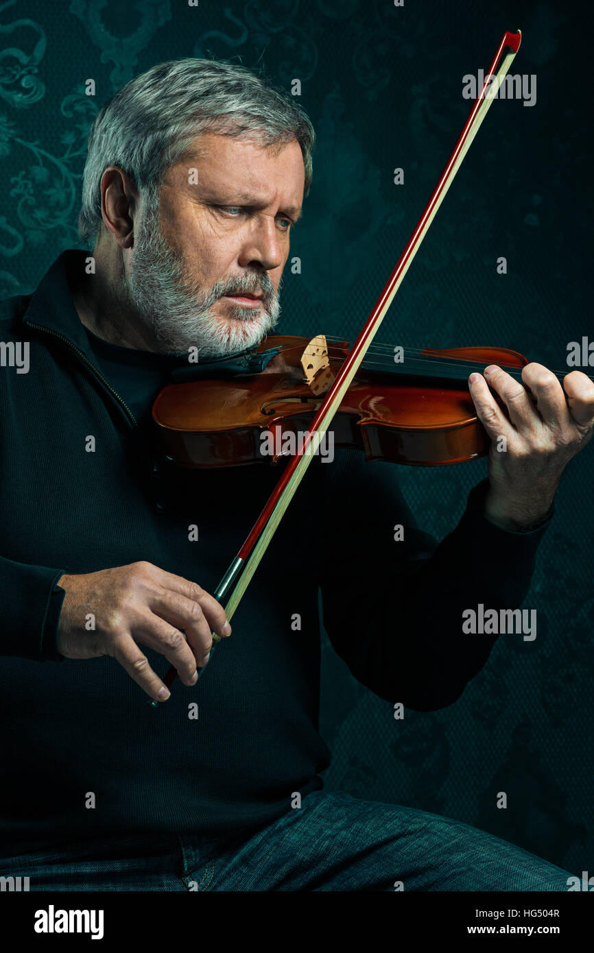 Senior musician playing a violin with a wand on black studio background ...