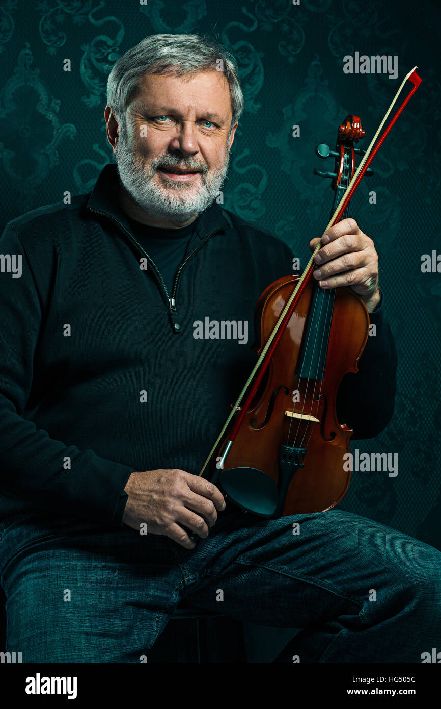 Senior musician playing a violin with a wand on black studio background ...