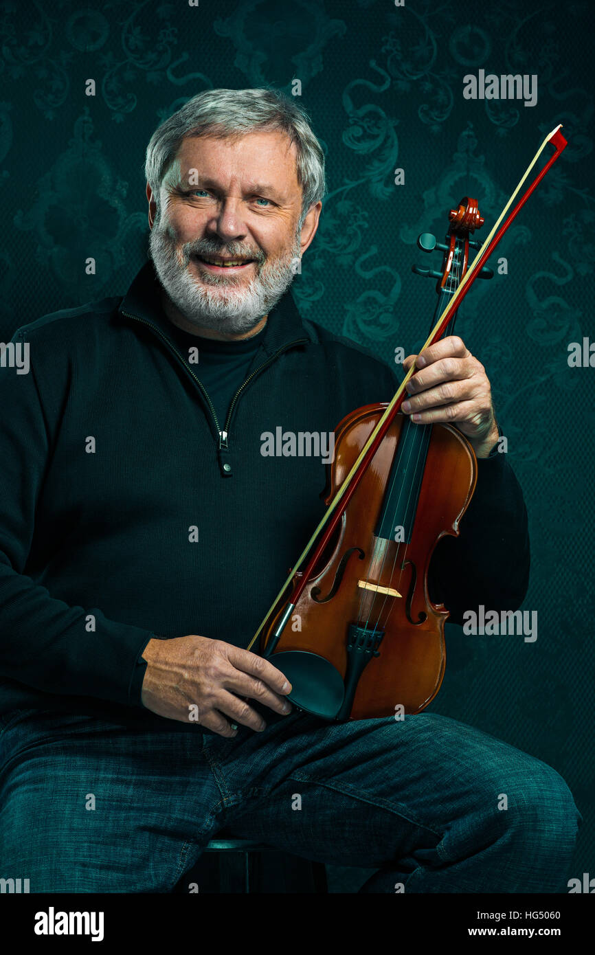 Senior musician playing a violin with a wand on black studio background ...