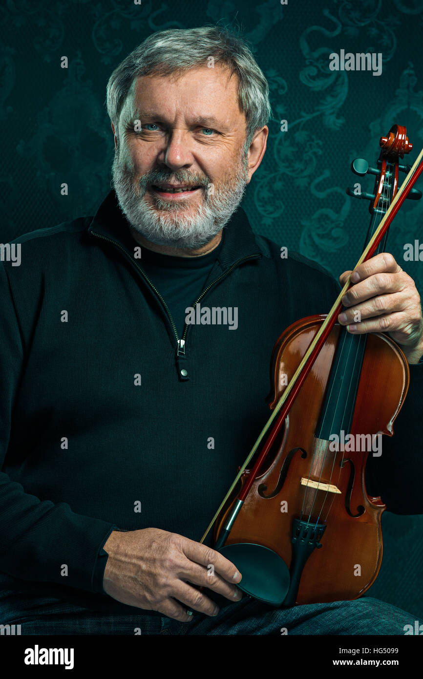 Senior musician playing a violin with a wand on black studio background ...