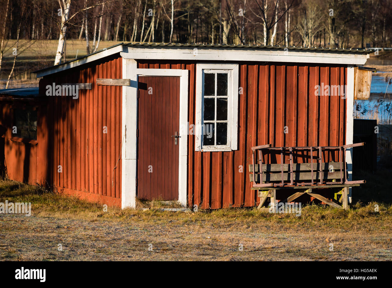 Small red wooden shed in the coastline. Bench outside and water in the ...