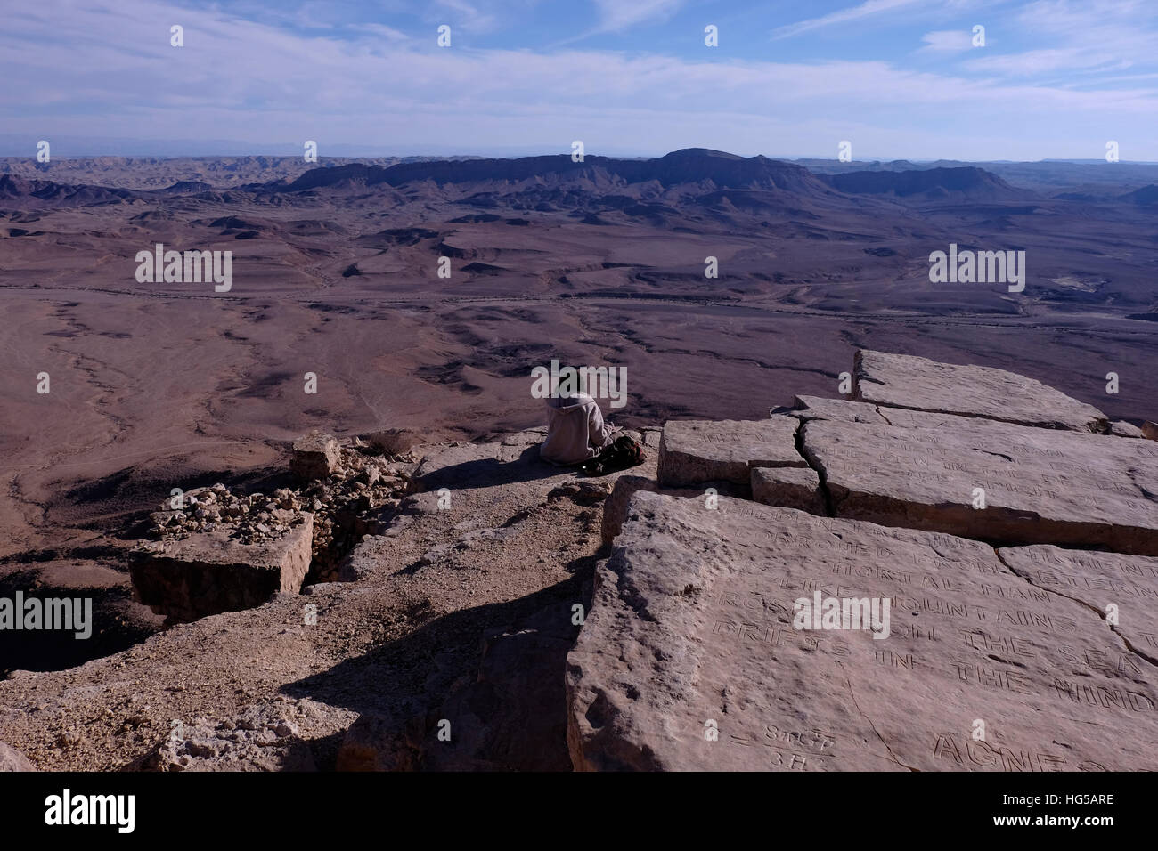 A lone female traveler sits on a cliff rim at the edge of Makhtesh ...