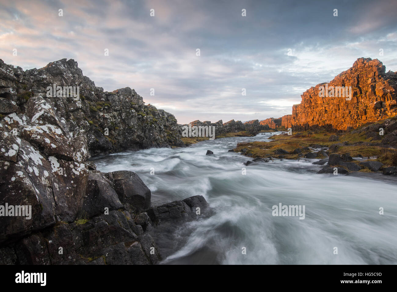 A river flows from the Oxarafoss waterfall at sunrise in Thingvellir ...