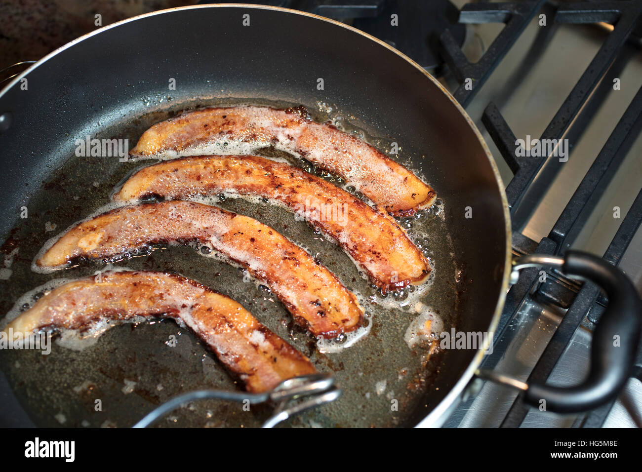 Four strips of bacon being fried in a pan to make Gumbo Stock Photo - Alamy