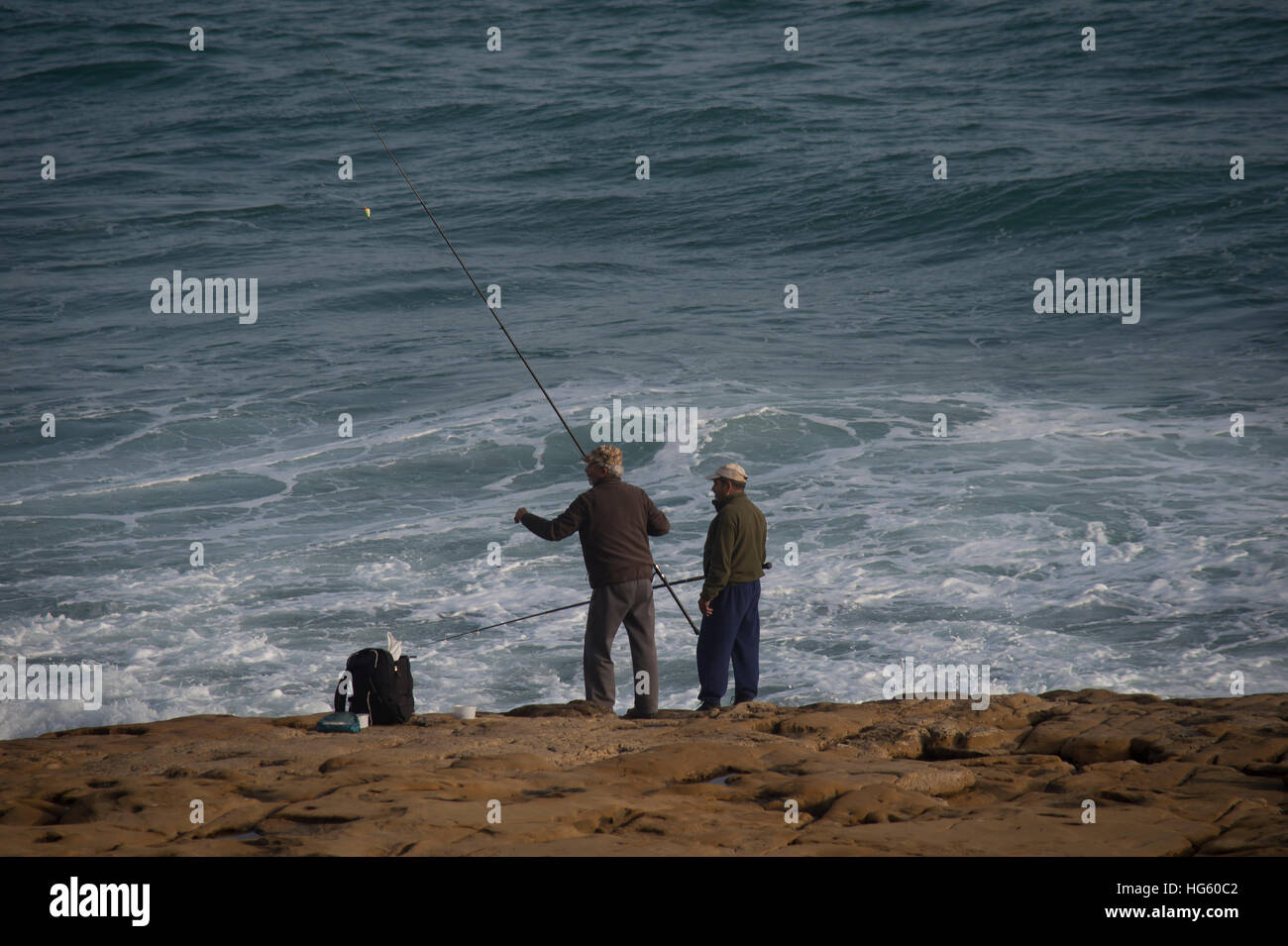 two men fishing off the rocks in Luz Portugal Stock Photo - Alamy