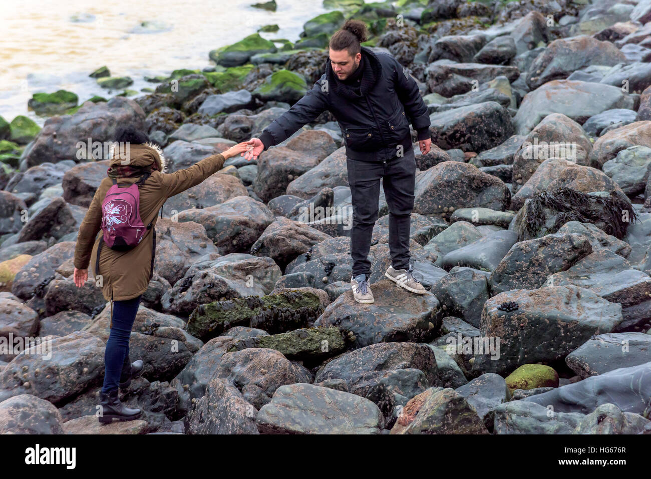 A young couple scramble over the rocks on the beach at St Ives in ...