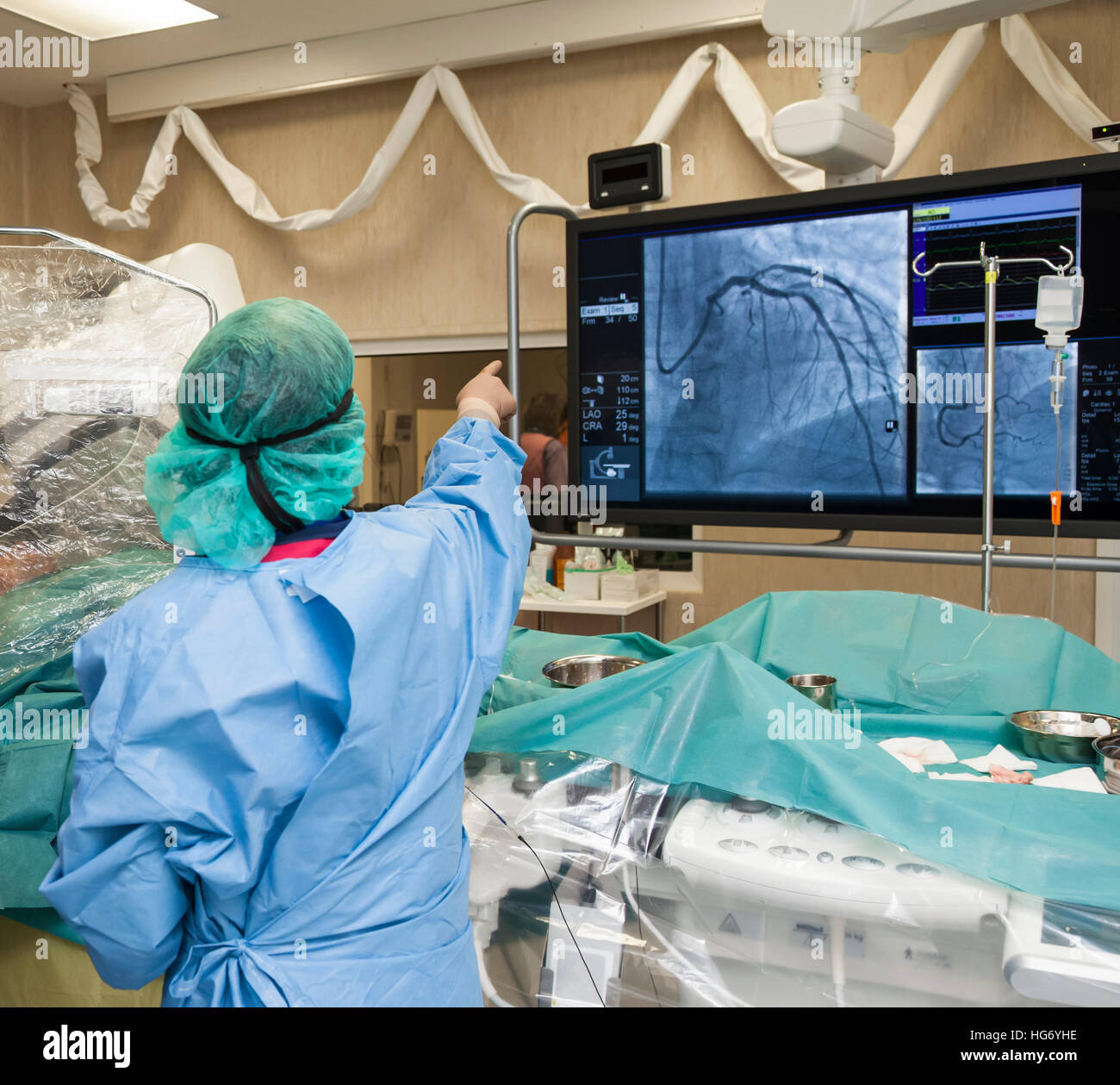 A surgeon with his back to the camera is pointing to a monitor during ...