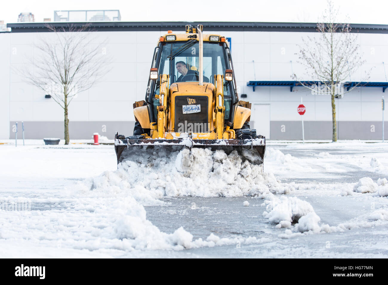 Backhoe clearing snow from a parking lot Stock Photo - Alamy