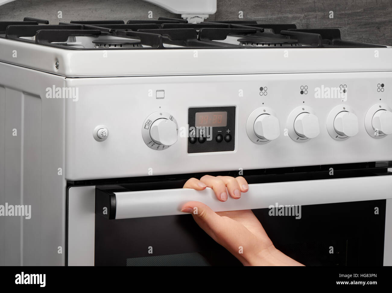 Female hand opening oven in white kitchen gas stove on gray background ...