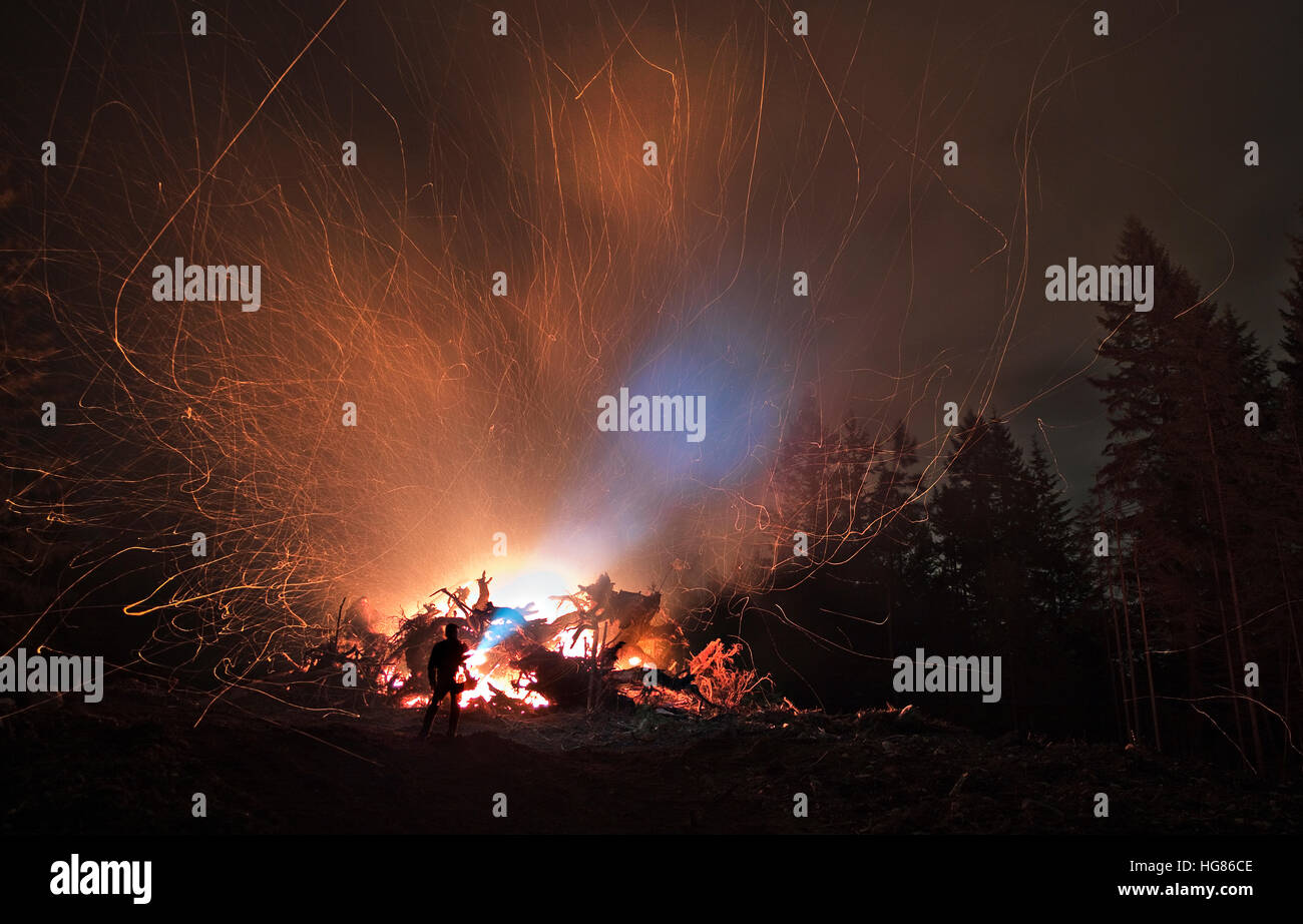 Rear view of man with flash light standing against fire in forest Stock ...