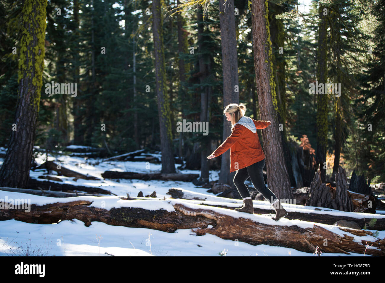 Side view of woman with arms outstretched walking on fallen tree trunk ...
