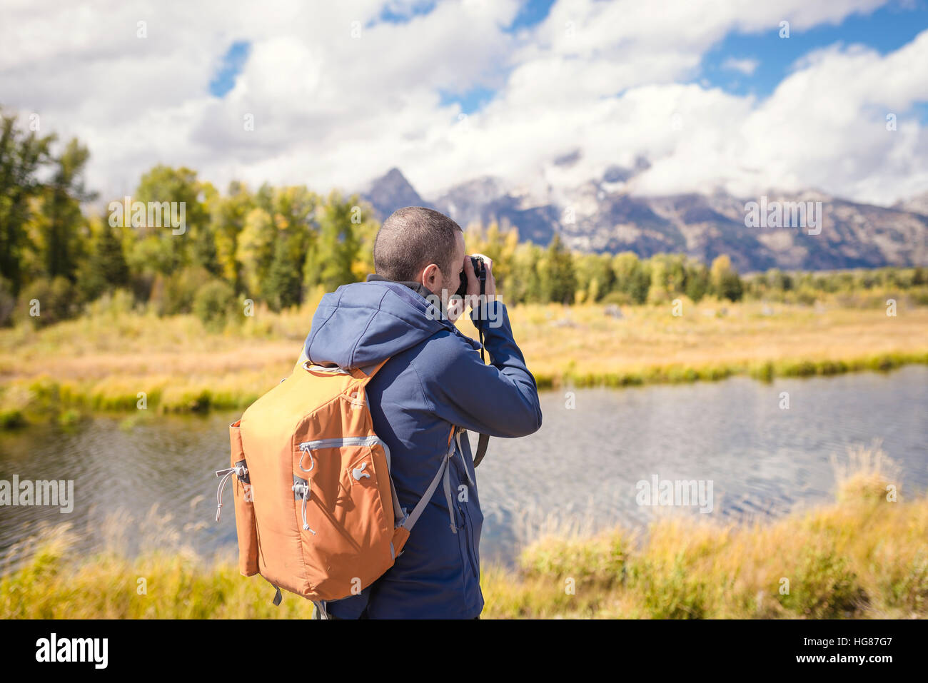 Man with backpack photographing while standing at riverbank Stock Photo ...