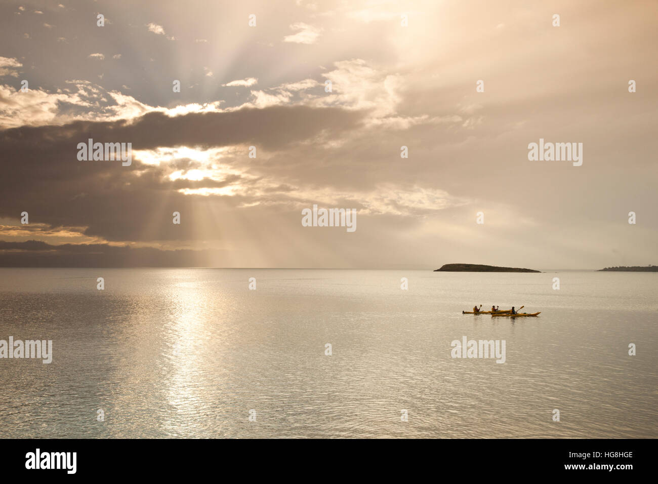 THREE kayakers on calm seas kayaking with sun behind clouds with god's ...