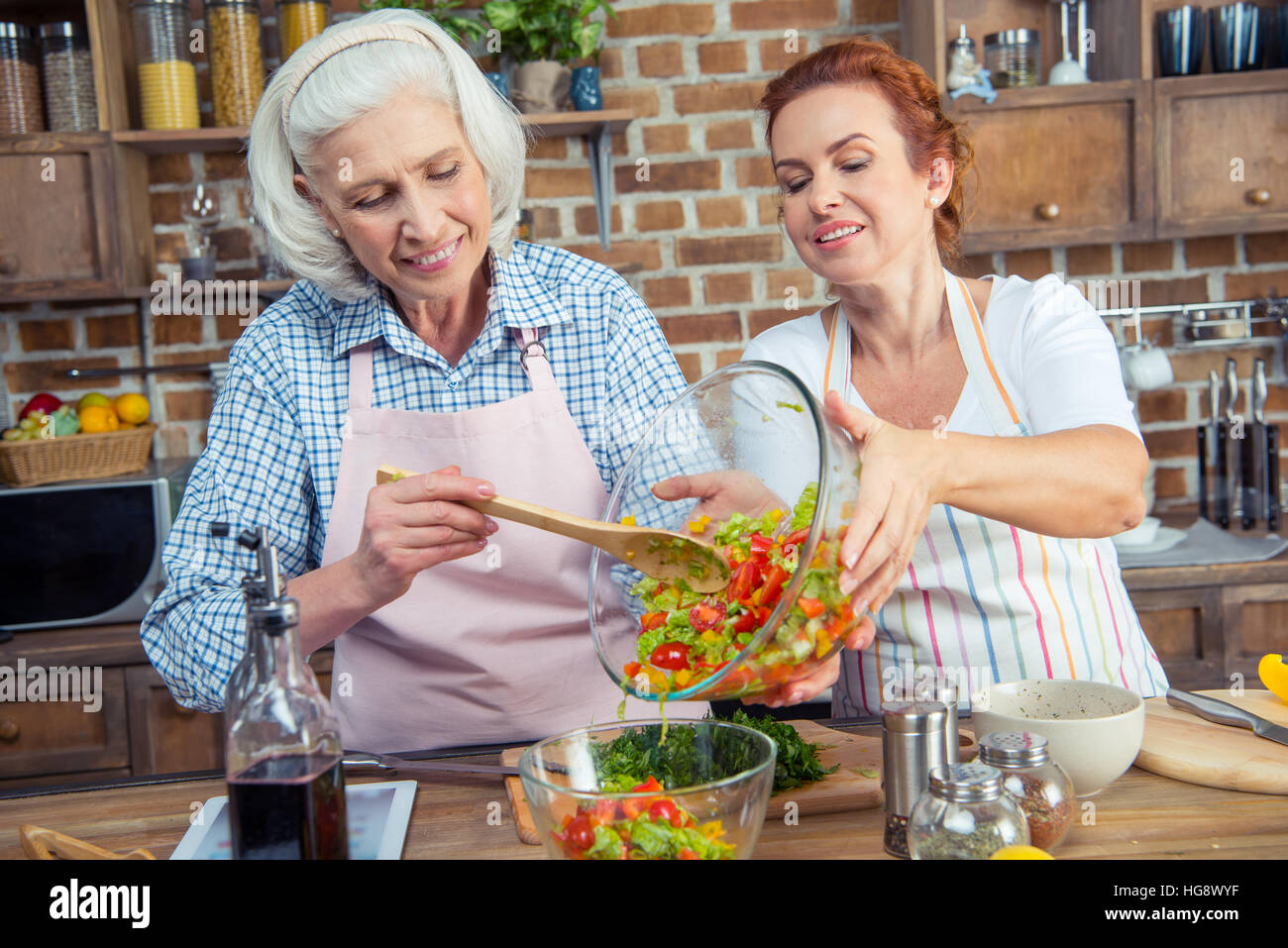 Two smiling women cooking vegetable salad together Stock Photo - Alamy