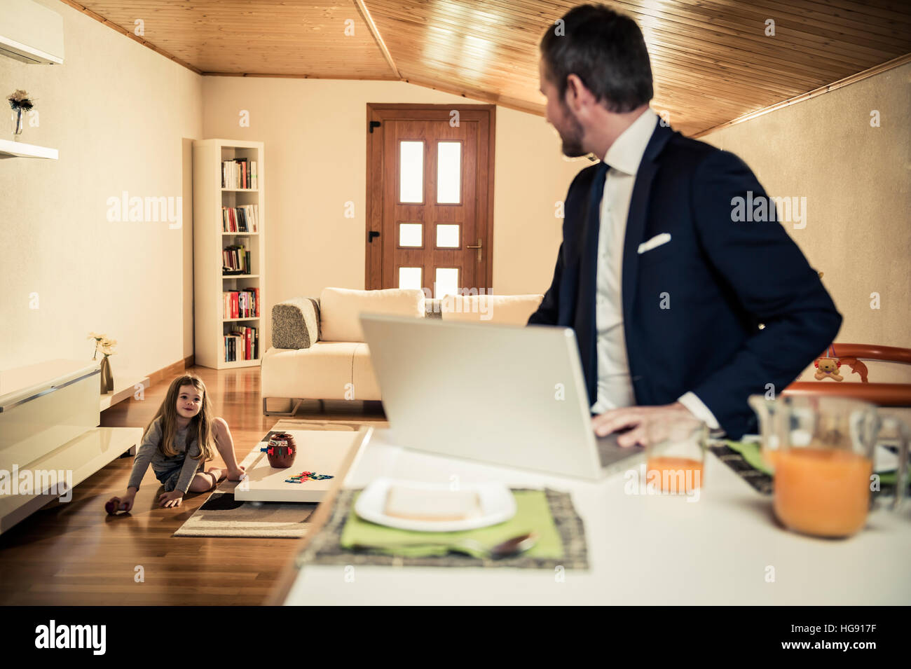 Young father working at home during breakfast while his little girl is ...