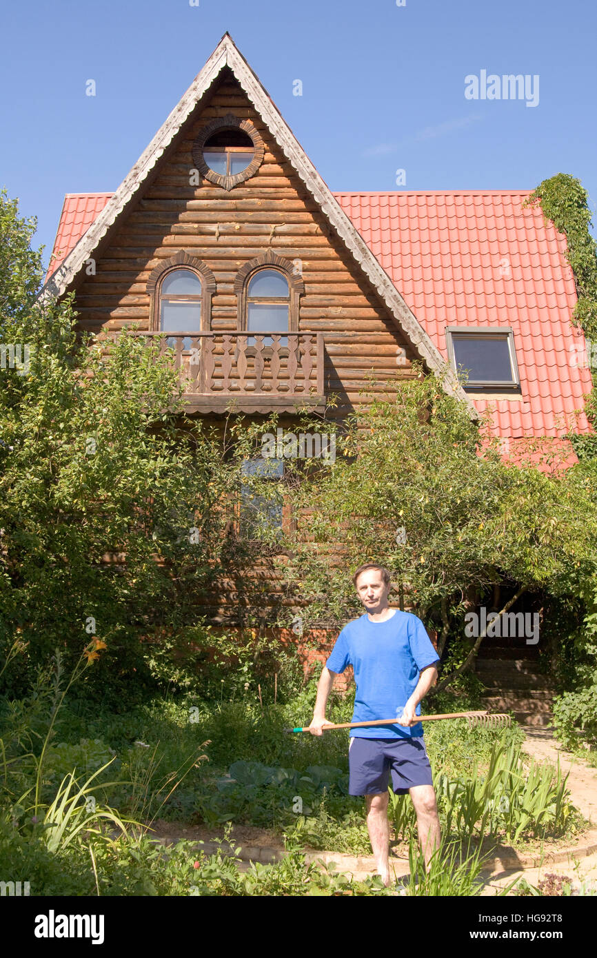 Man with rake in hands standing near his country house in garden Stock ...