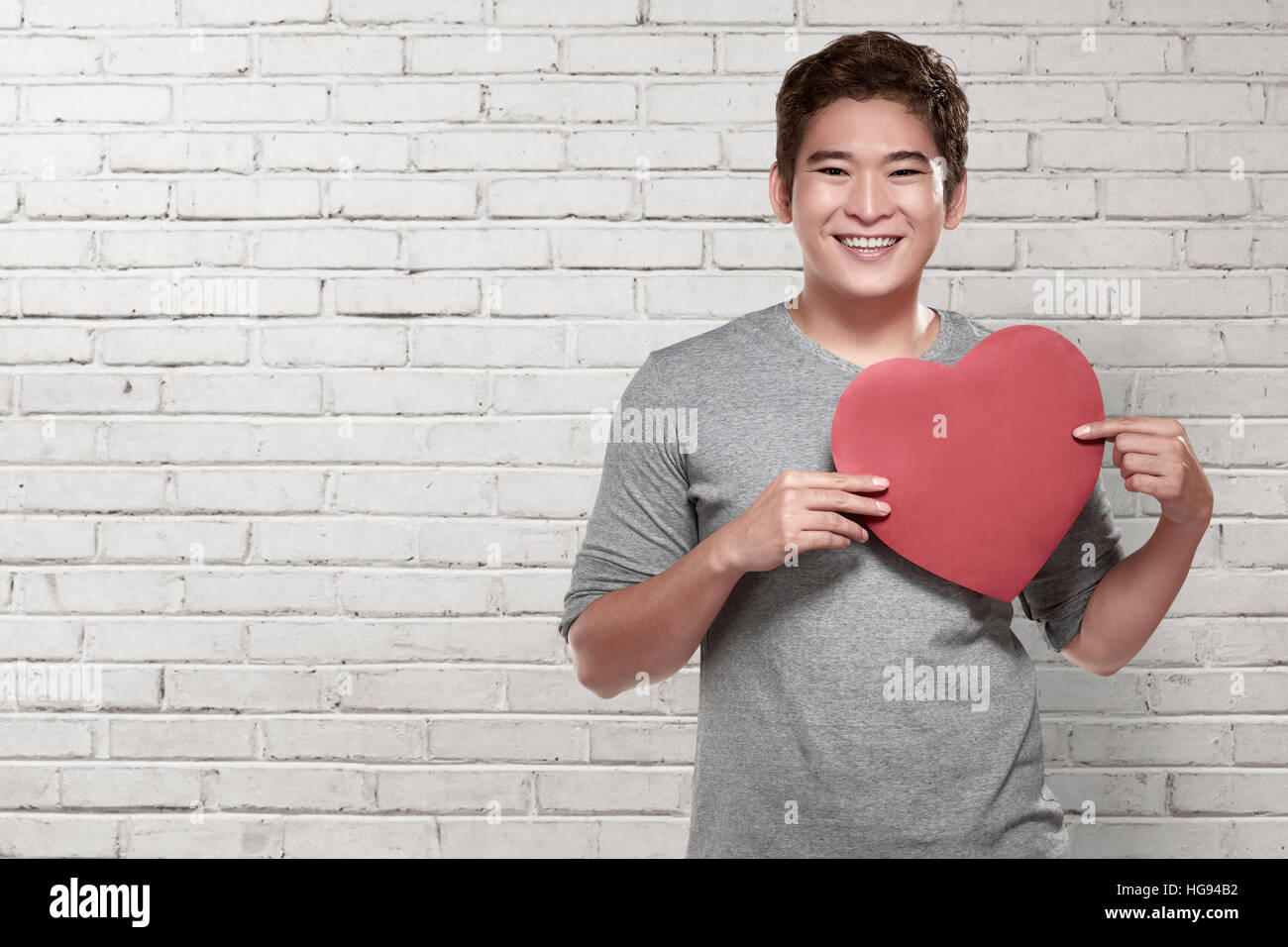 Handsome asian man holding red heart symbol on wall background Stock ...