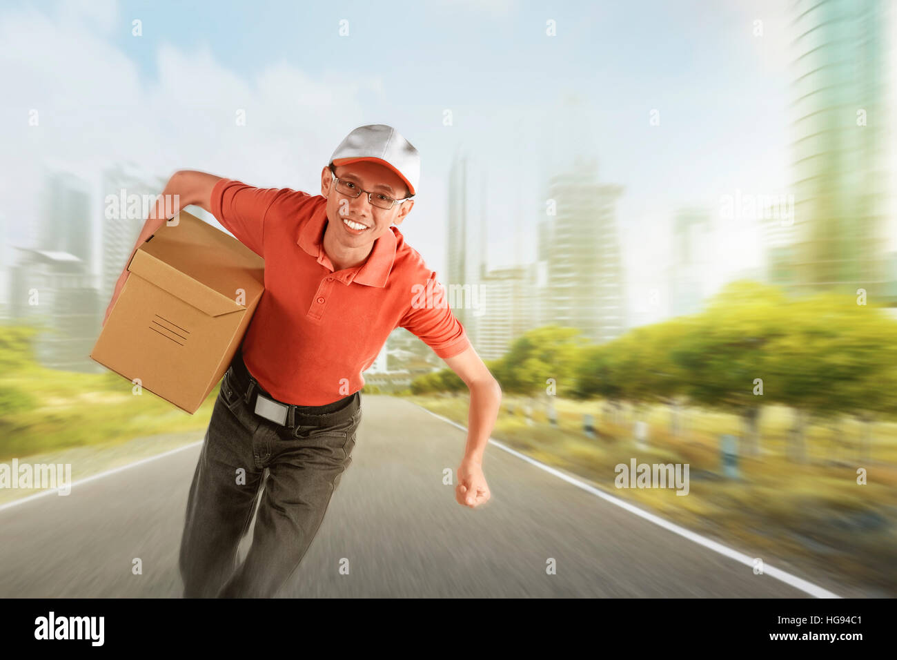 Attractive asian courier delivering package over blurred city ...