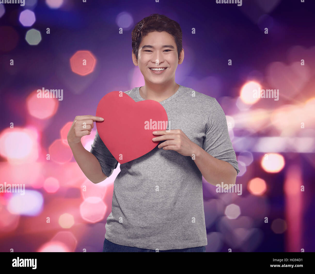 Portrait of asian man holding red heart shape over blurred light ...