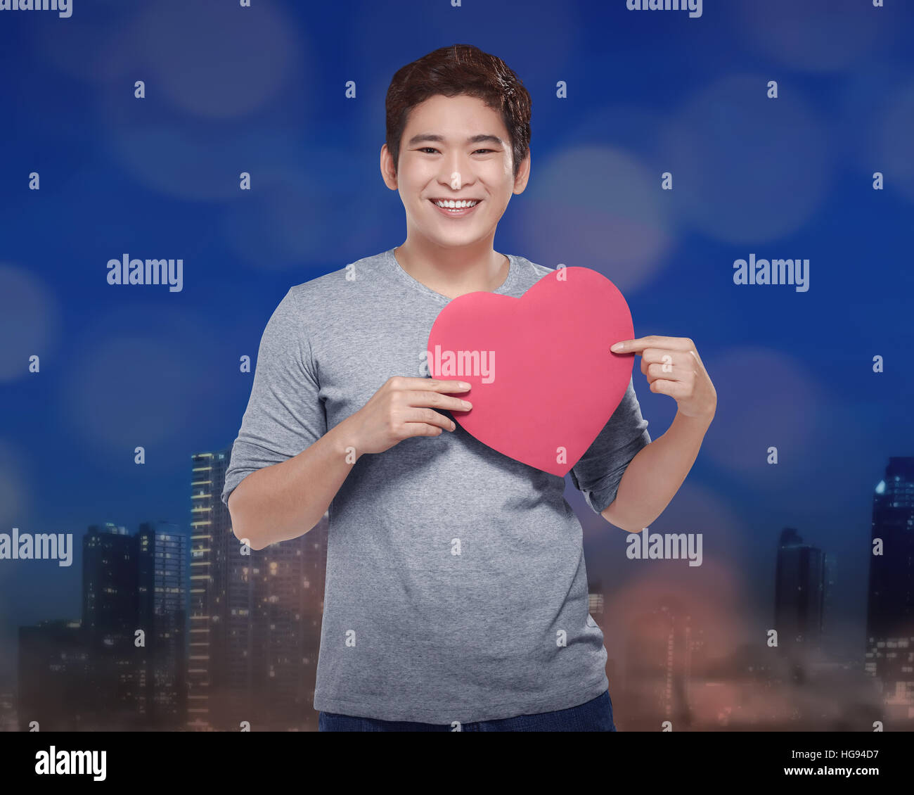 Attractive asian man holding heart in his hand with night city ...