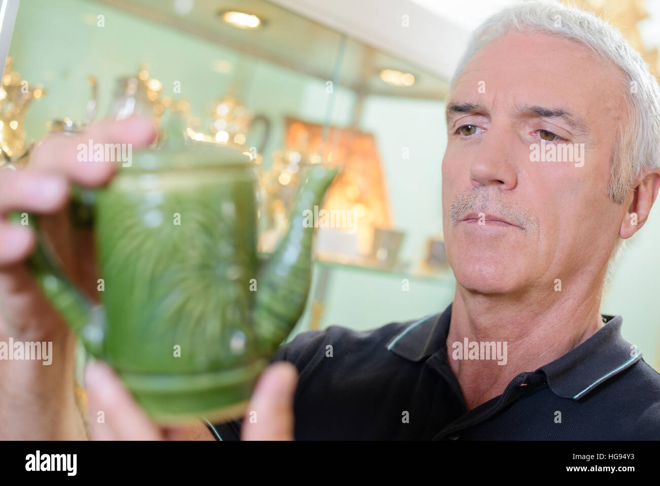 Man looking at antique tea pot Stock Photo - Alamy