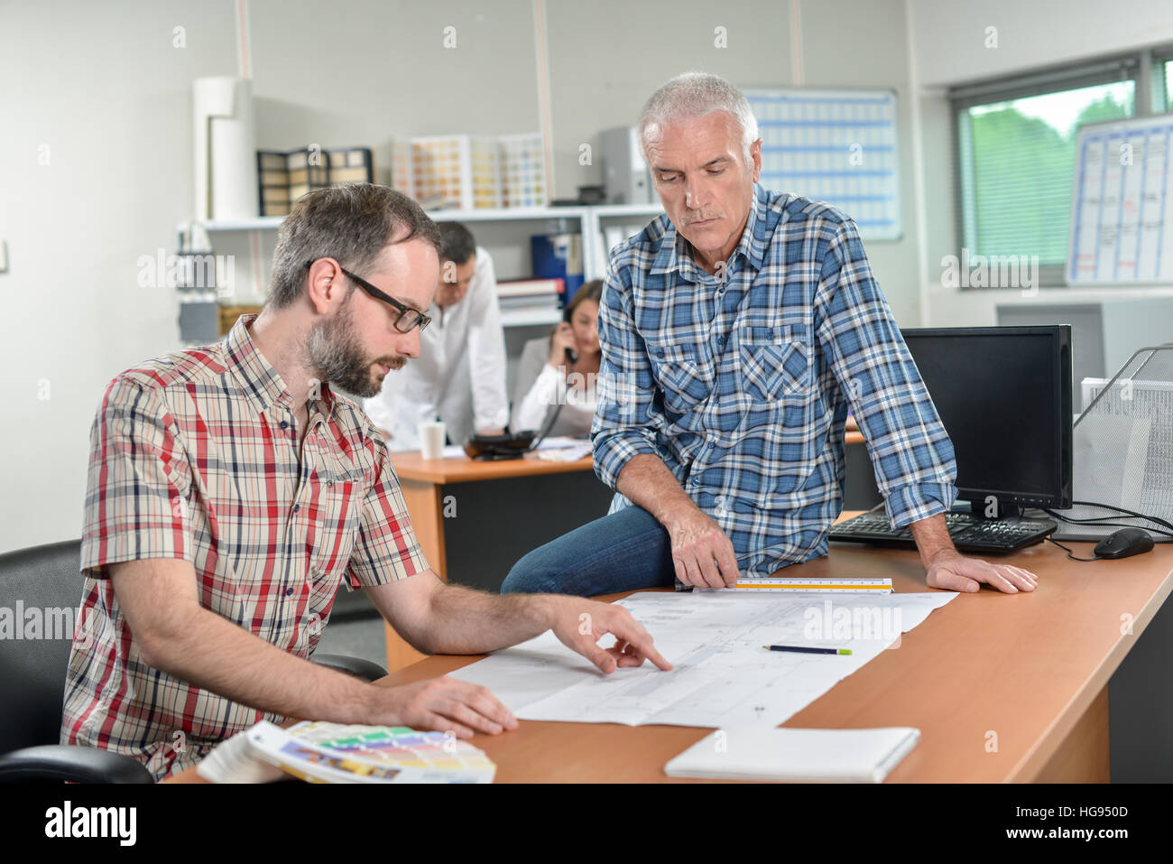 Two men looking at paperwork, one sat on the table Stock Photo - Alamy