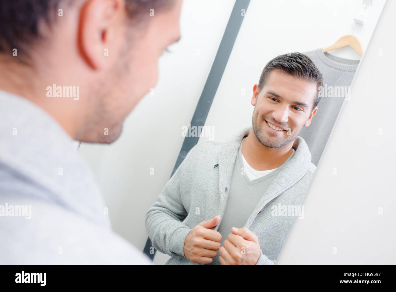 Man trying on jacket, looking at reflection in mirror Stock Photo - Alamy
