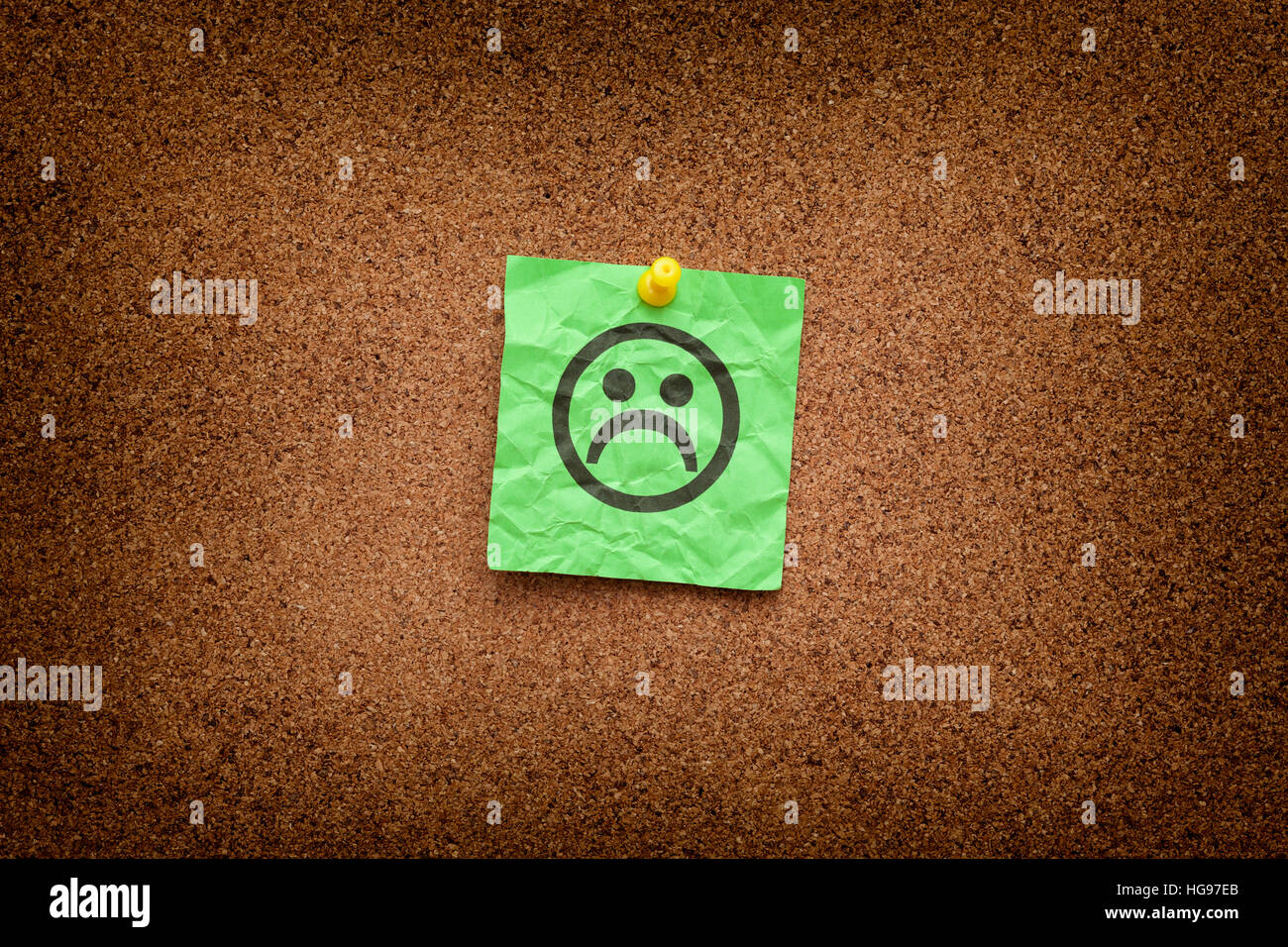 Green paper note with sad face on a cork board. Depression concept ...