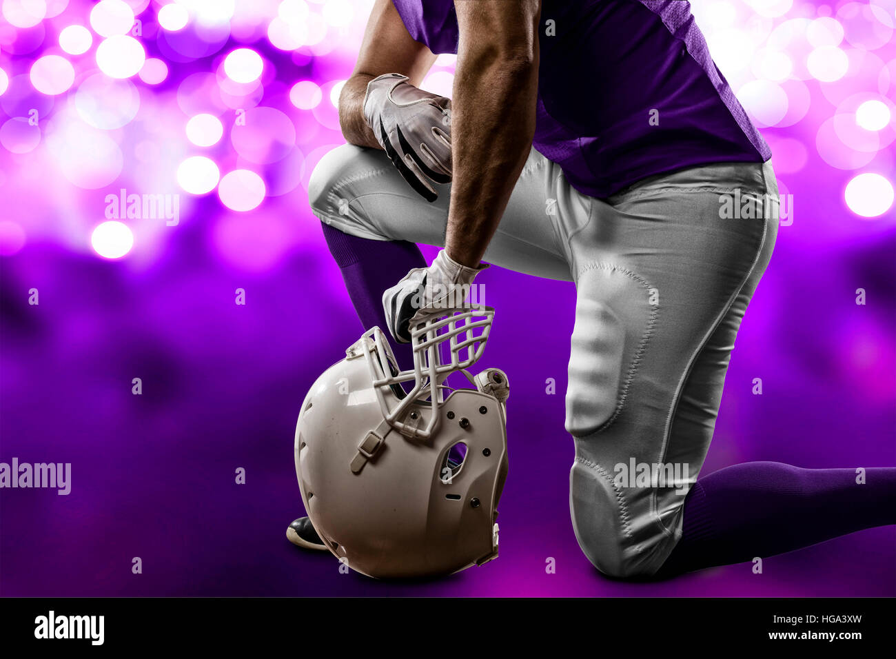 Football Player with a purple uniform on his knees, on a purple lights ...