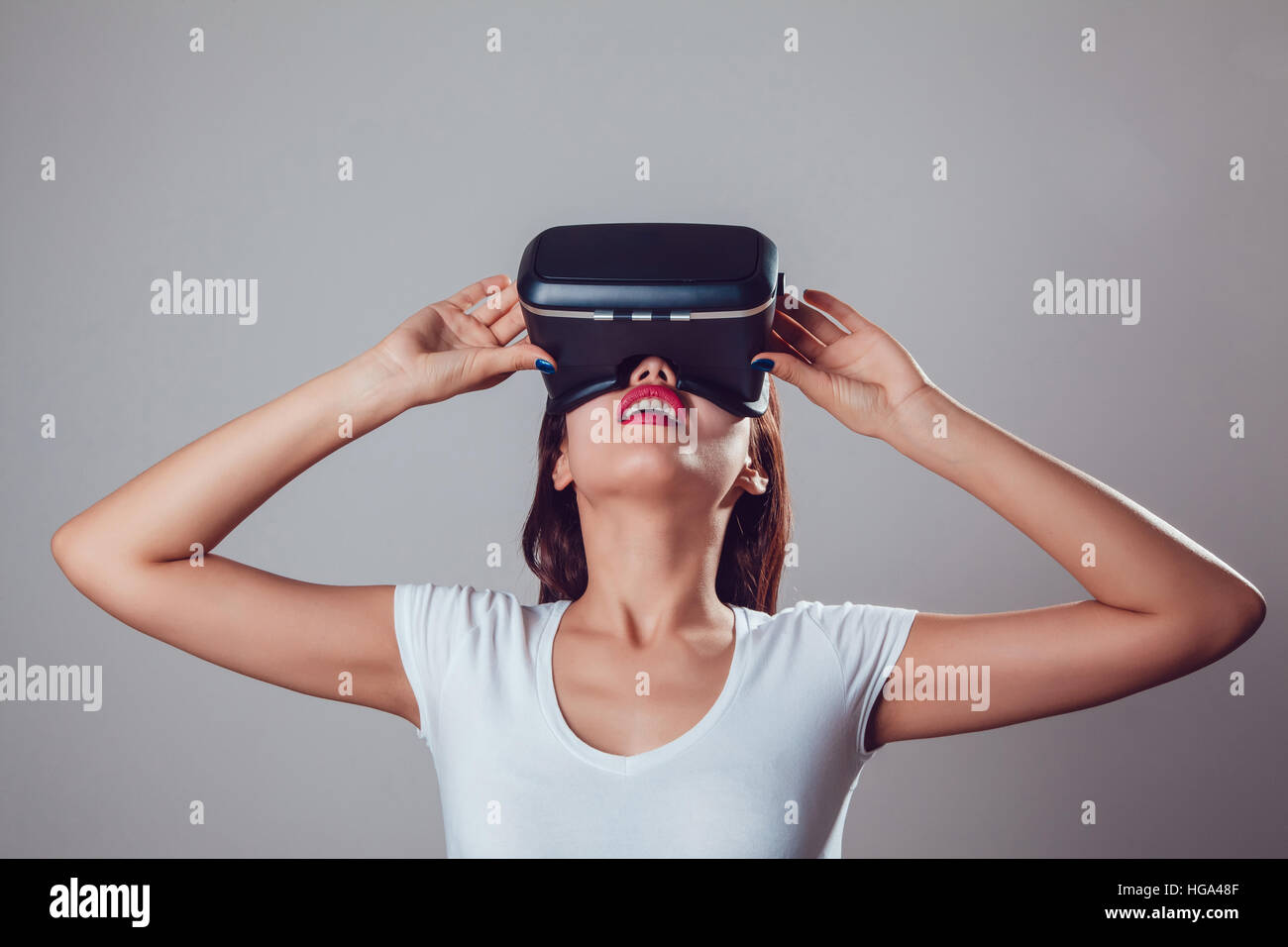 Attractive woman wearing virtual reality goggles. VR headset. Virtual reality concept on grey ...