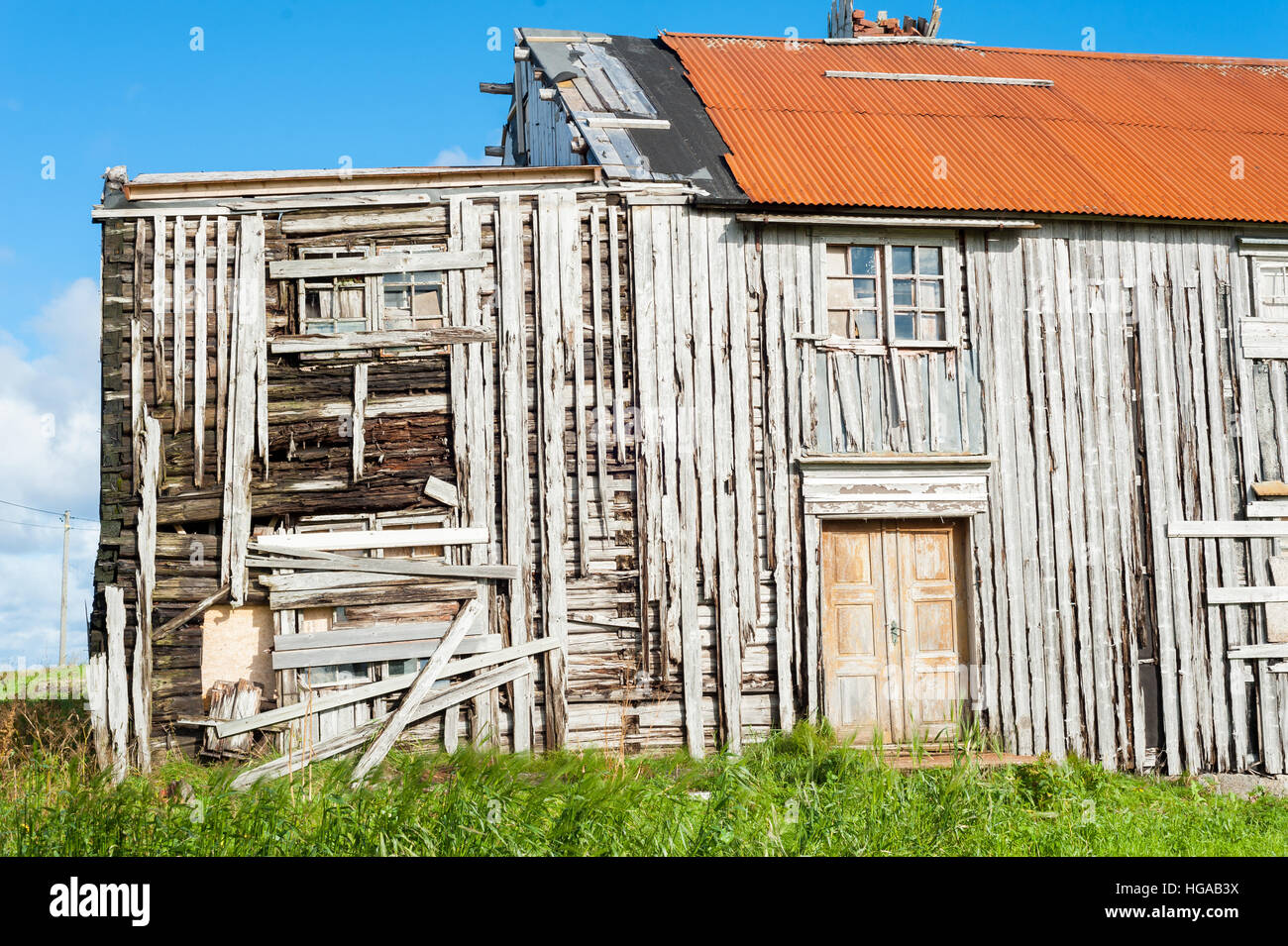 Side view of an old and derelict wooden house with red roof and broken ...