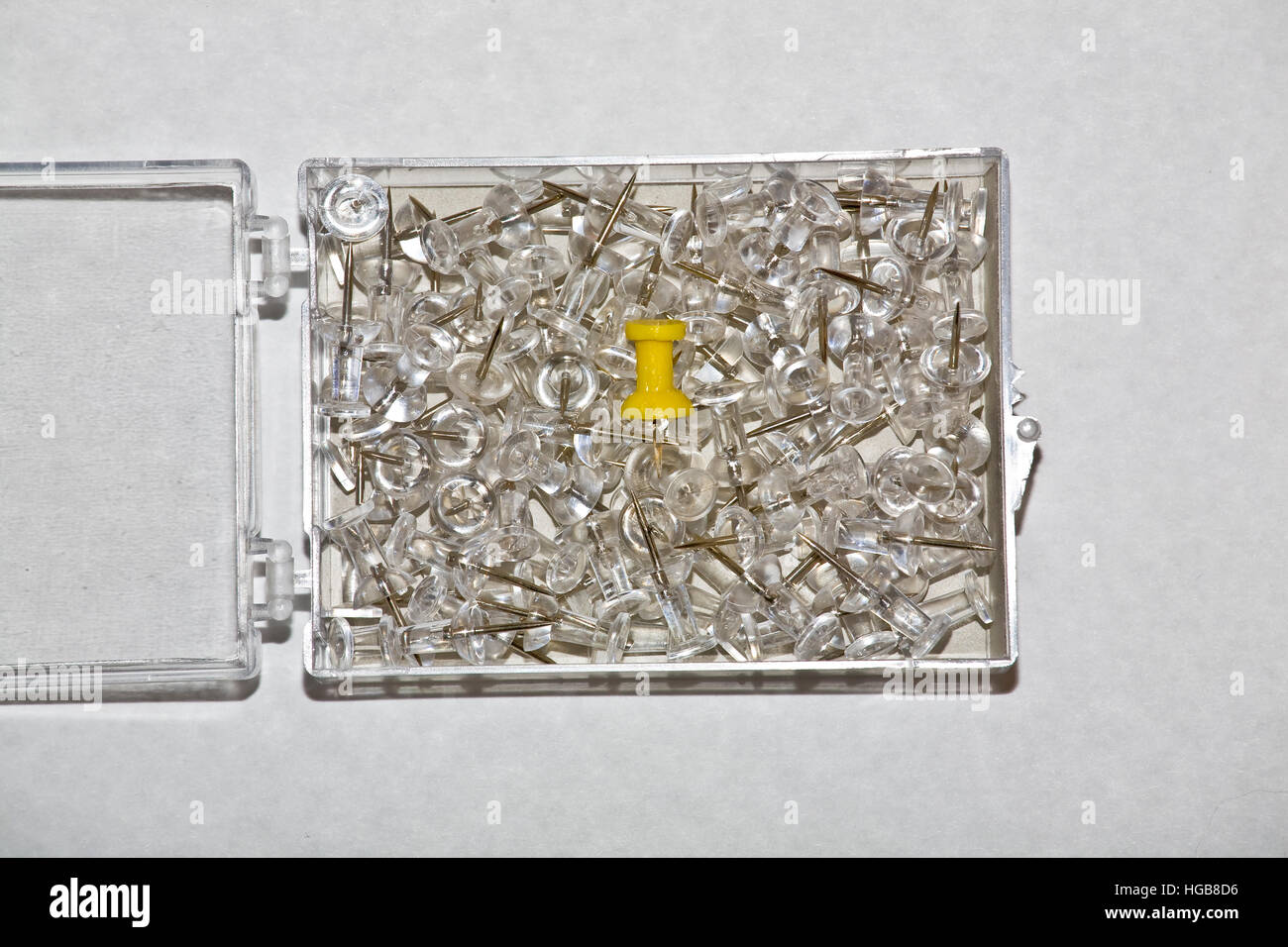 Single yellow colored push pin in box of transparent pins. This can ...