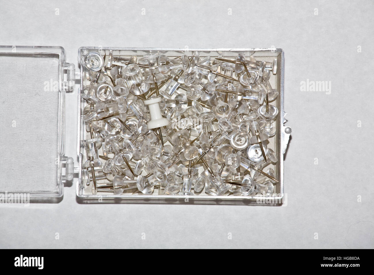 Single white colored push pin in box of transparent pins. This can ...