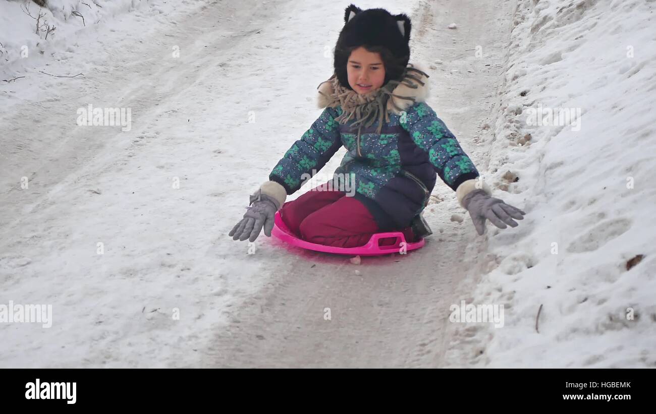 little girl riding snow slides rolling down the hills, winter time ...