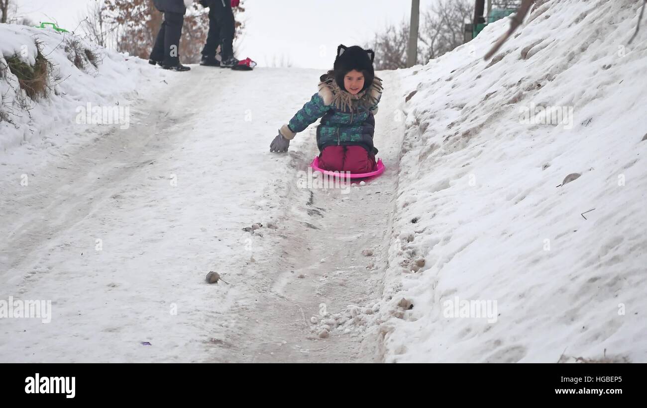 little girl riding snow slides rolling down the hills, winter time ...