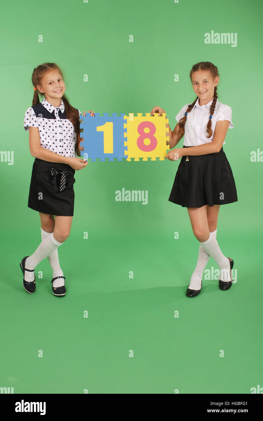 Two school girls hold color board with the number eighteen on green ...