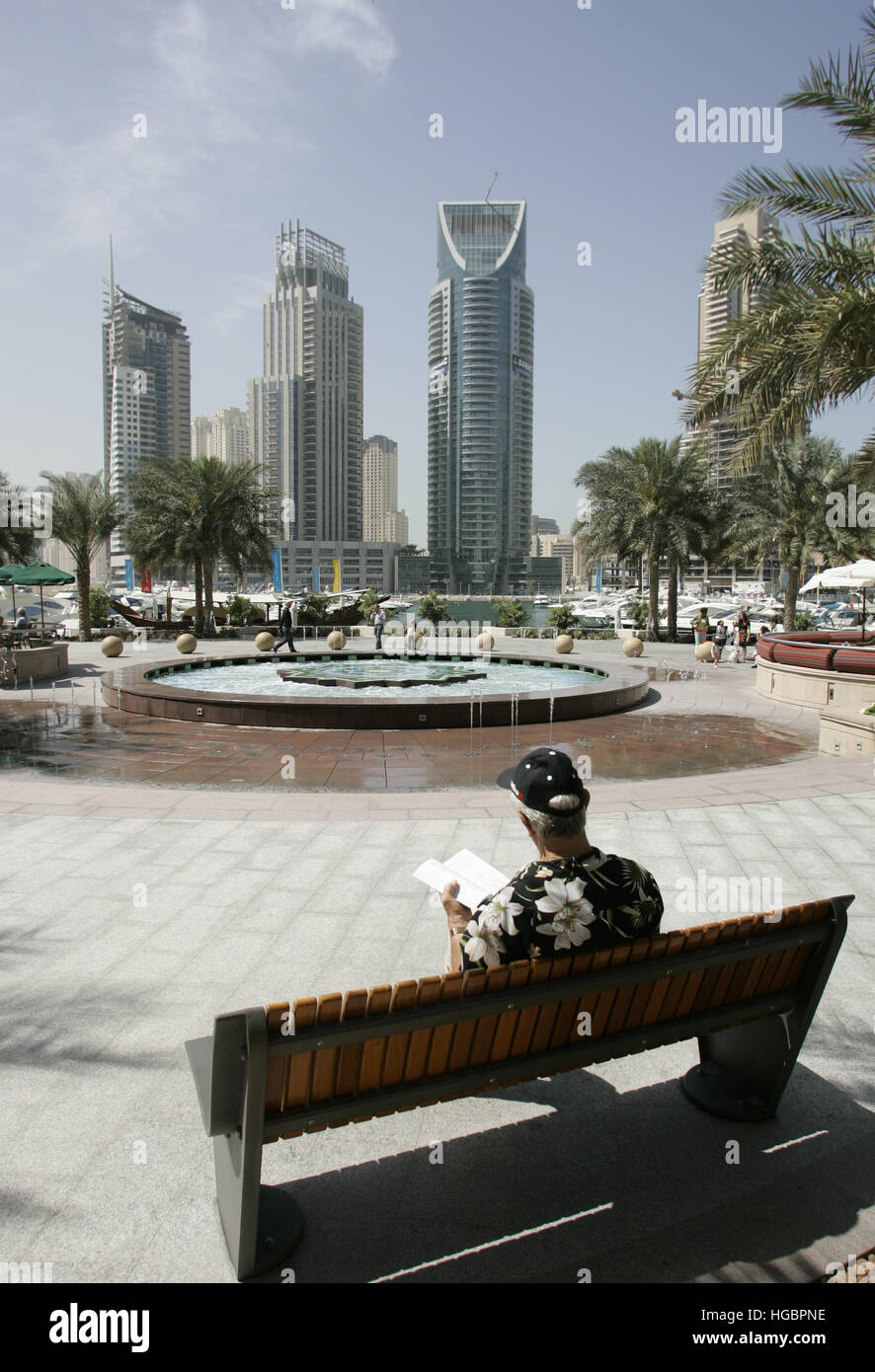 U.A.E., Dubai, Tourist sitting on a bench reading a travel guide and ...