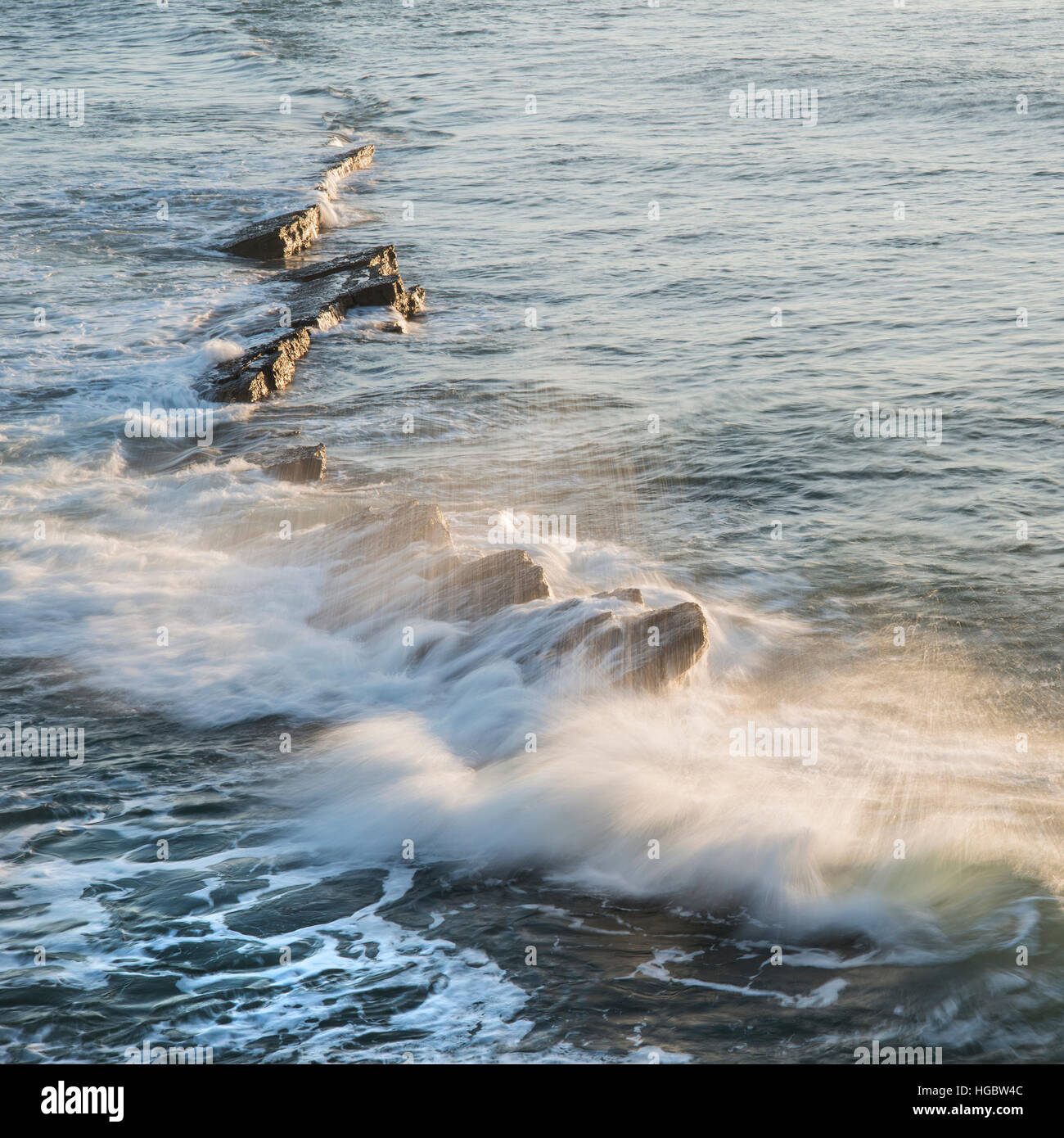 Wave crashing over rocks in ocean at sunrise Stock Photo - Alamy