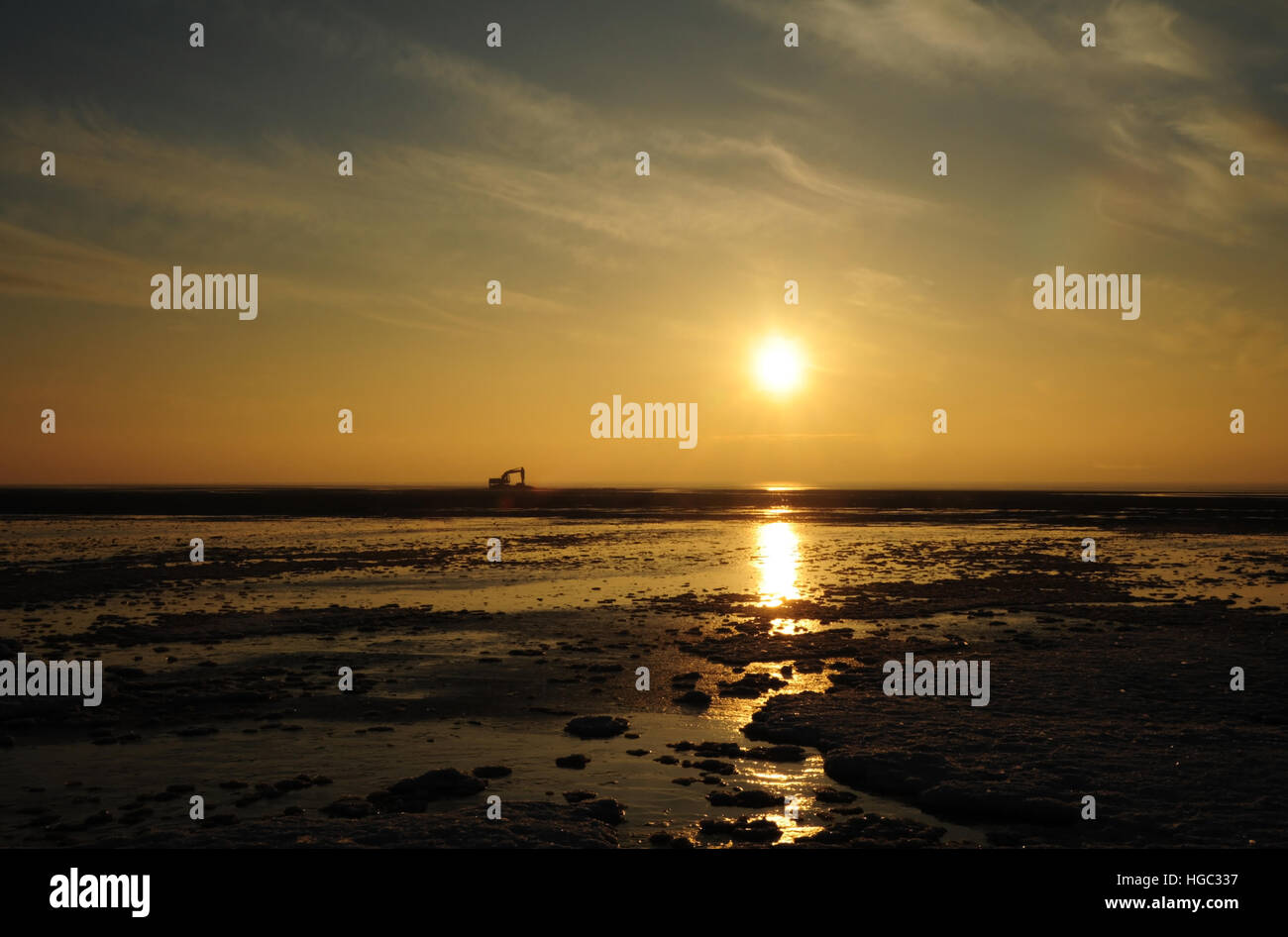 View across sea ice sand beach to sand-winning digger and yellow sky ...